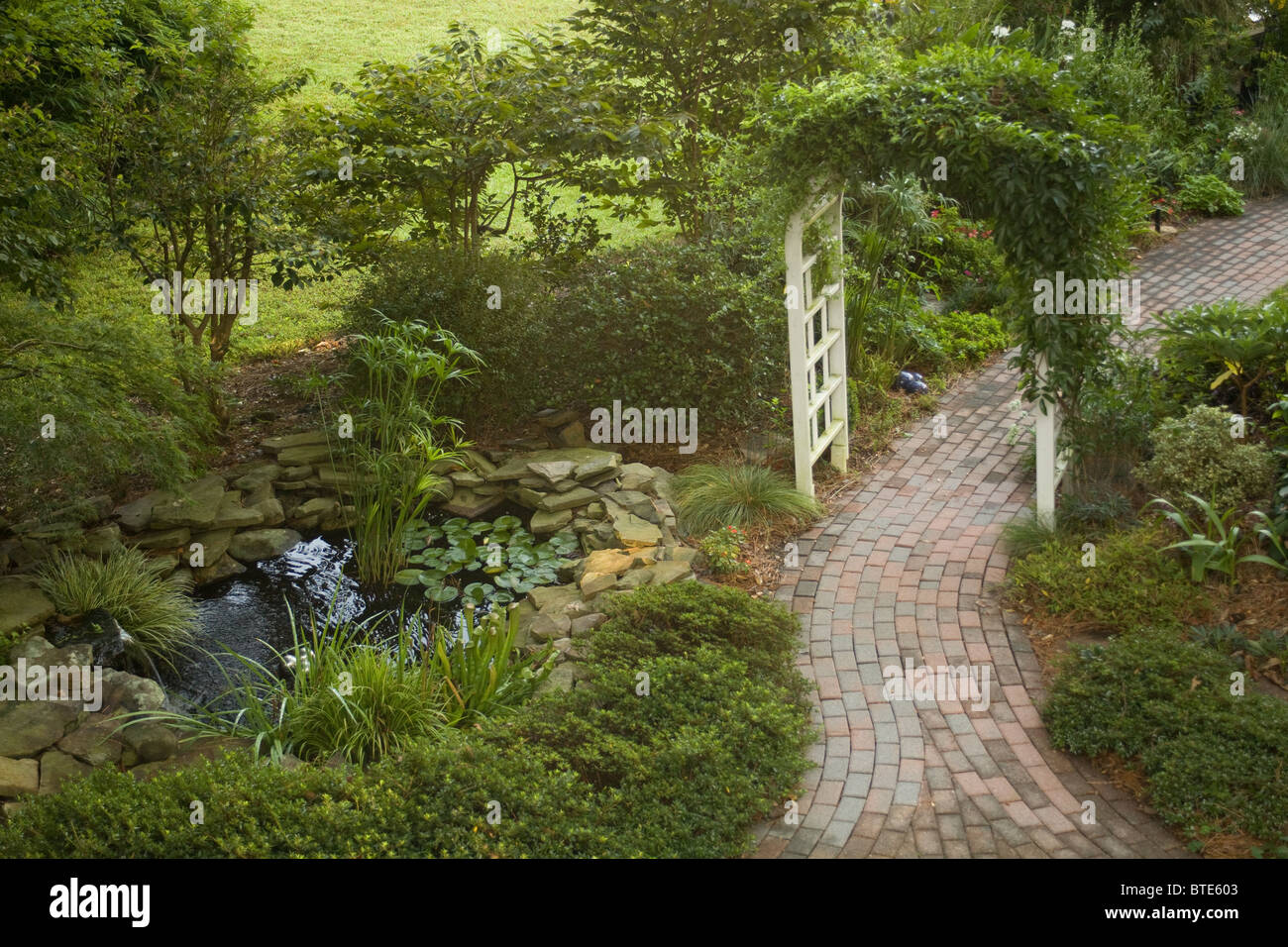View of the garden pond and trellis with brick path Stock Photo - Alamy
