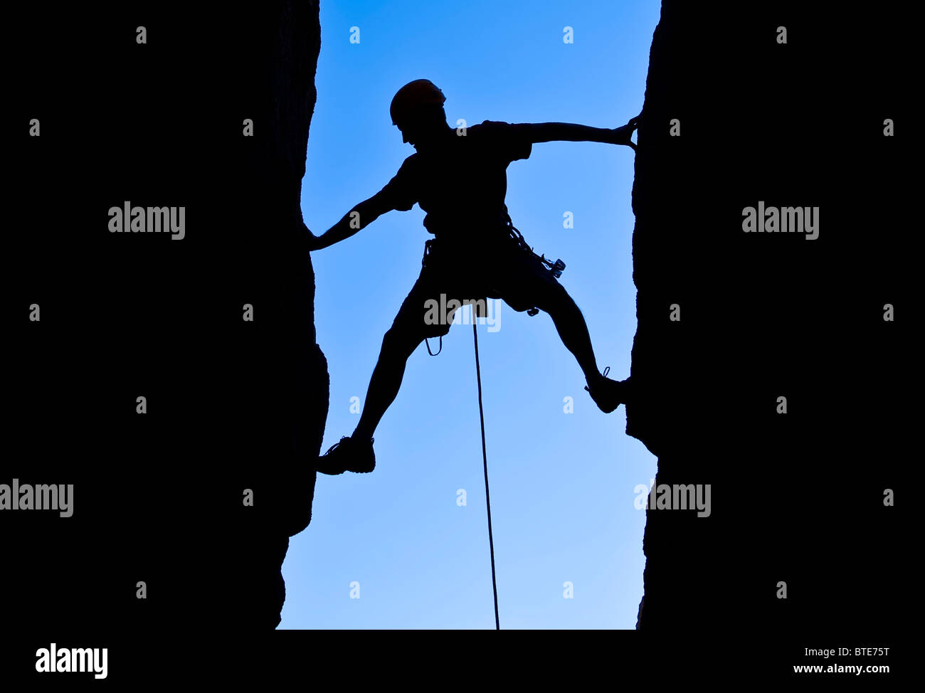 Rock climber silhouetted as he climbs up a chimney in Joshua Tree ...