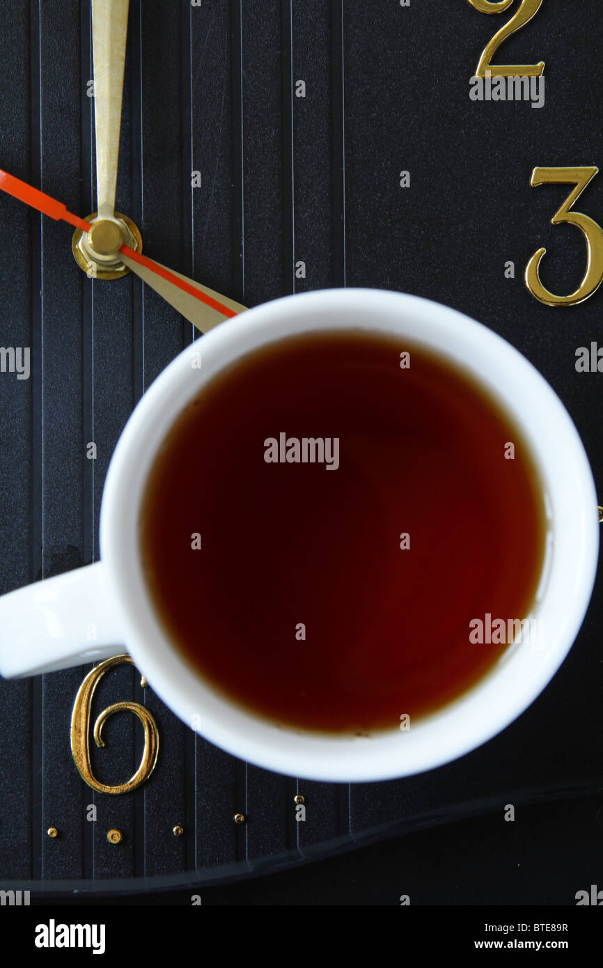 Big black clock and a cup of tea Stock Photo - Alamy