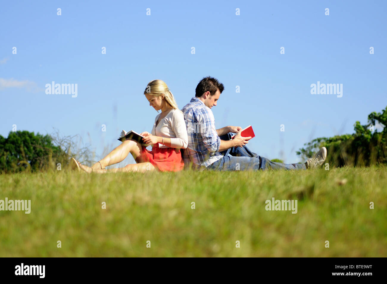 Couple sitting back to back reading in park Stock Photo - Alamy