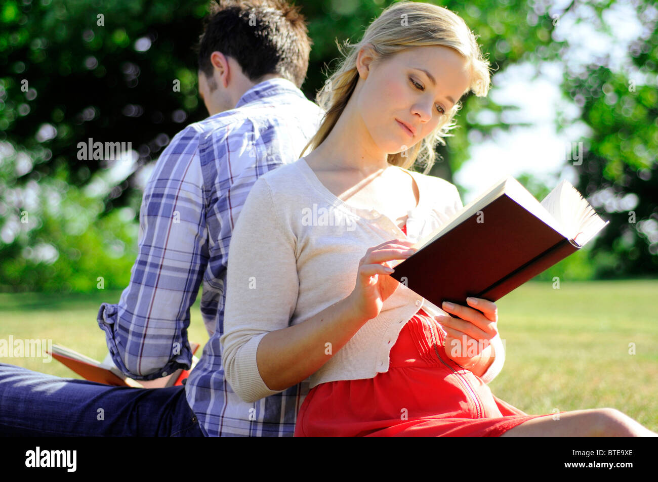 Couple sitting back to back reading in park Stock Photo - Alamy
