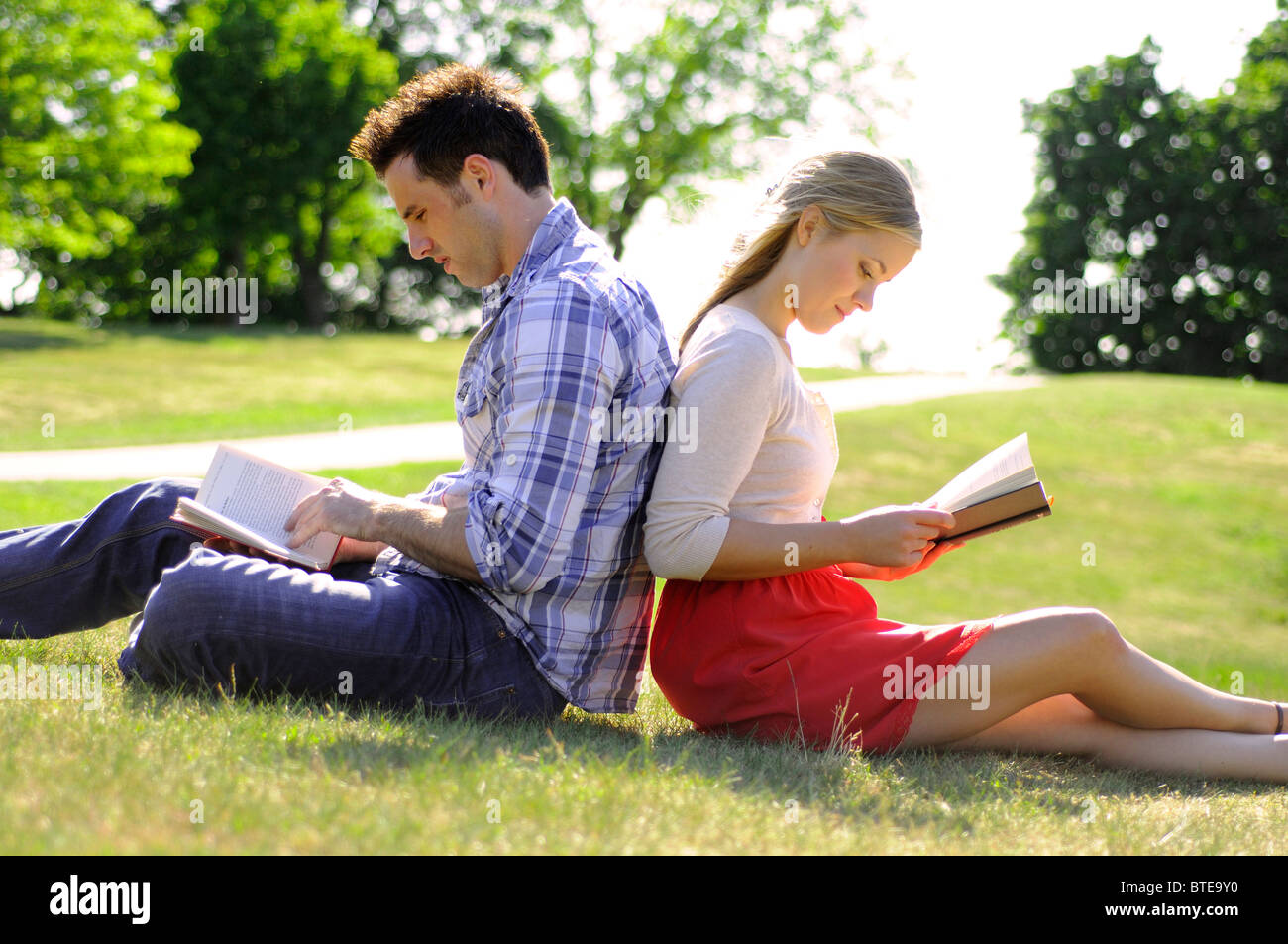 Couple sitting back to back reading in park Stock Photo - Alamy
