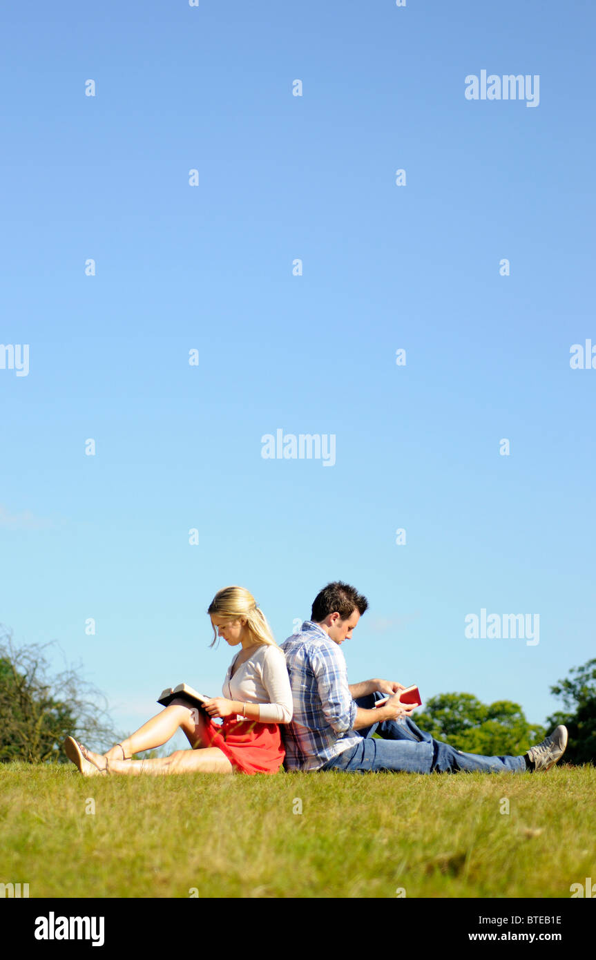 Couple sitting back to back reading in park Stock Photo - Alamy