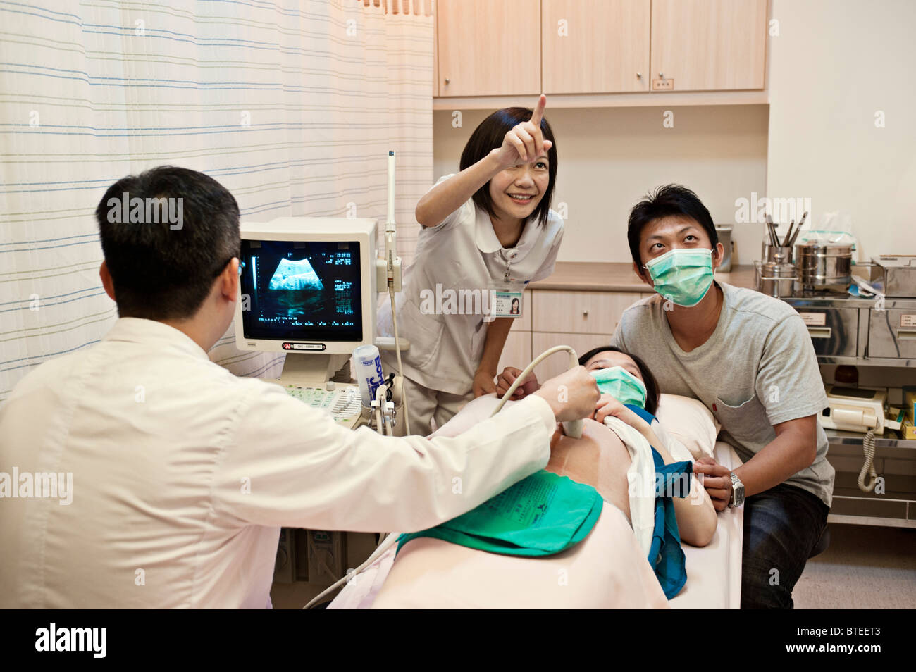 Doctor performing ultrasound on pregnant woman and looking at sonogram ...