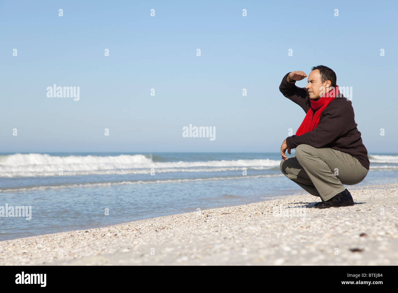 Man crouching on beach, looking at ocean Stock Photo - Alamy