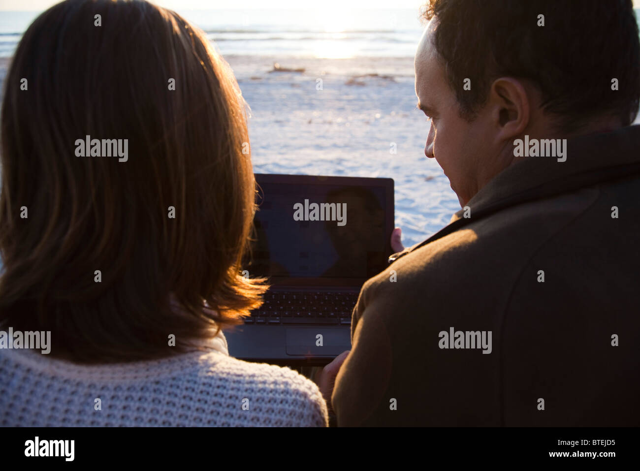 Couple using laptop computer together at the beach Stock Photo - Alamy