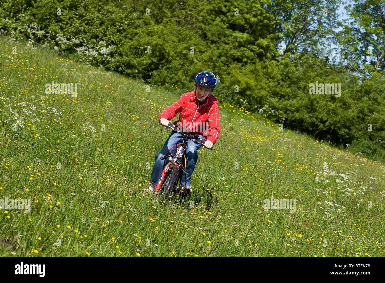 A young teenage boy riding his mountain bike in a field of buttercups ...