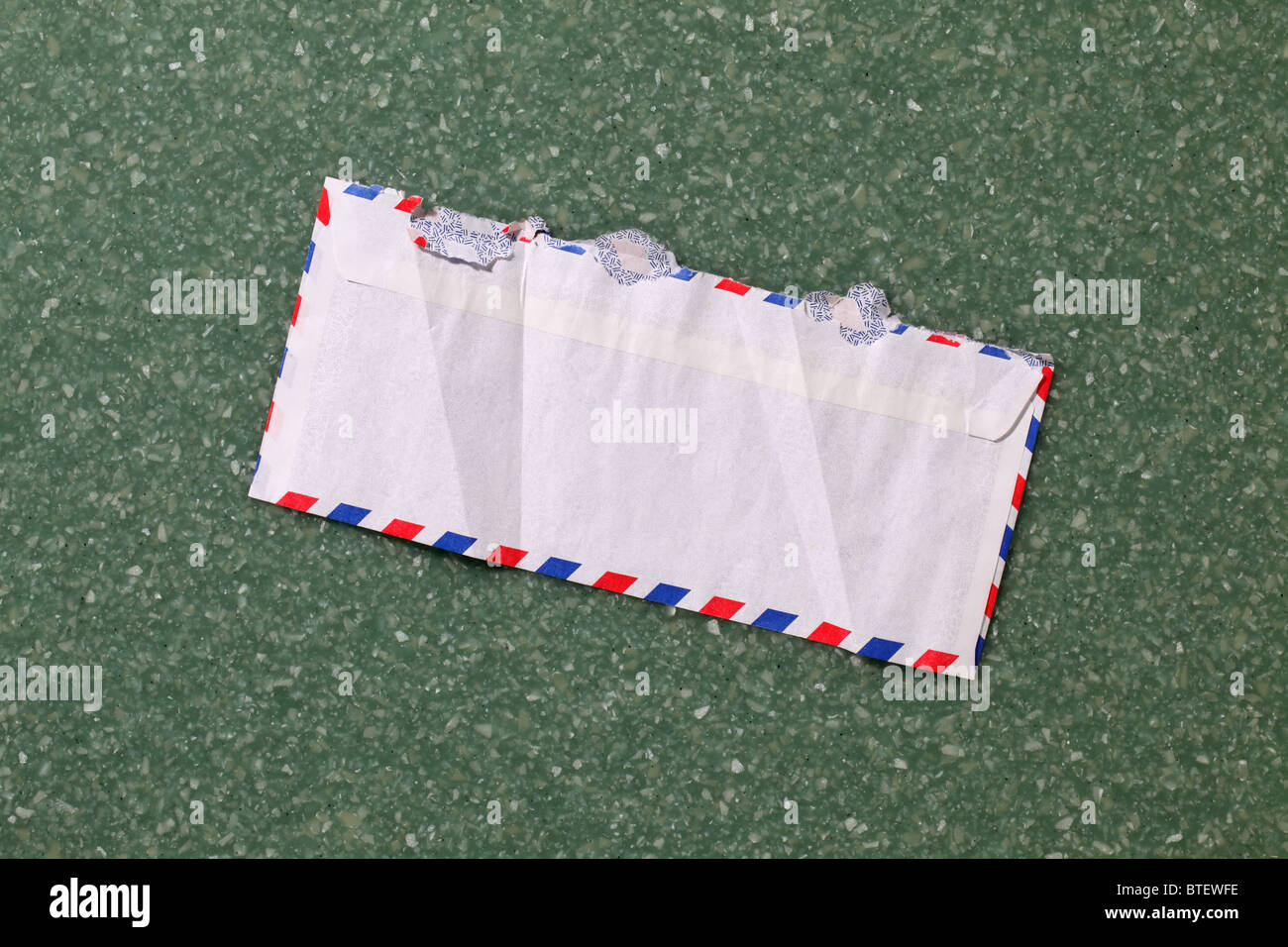 A used postal mailing envelope torn open. Green speckled counter top ...