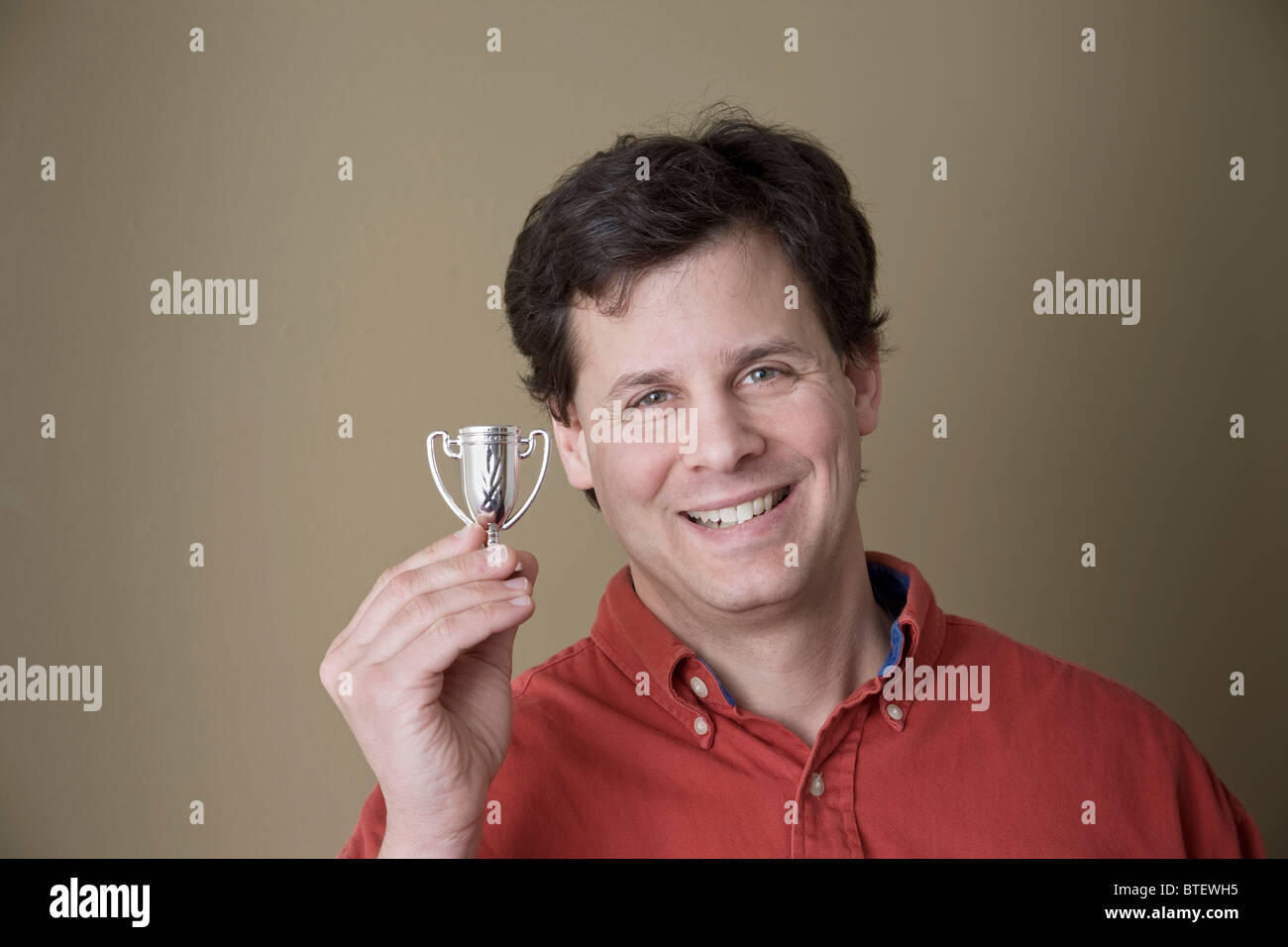 Man smiling holding a very small trophy cup Stock Photo - Alamy