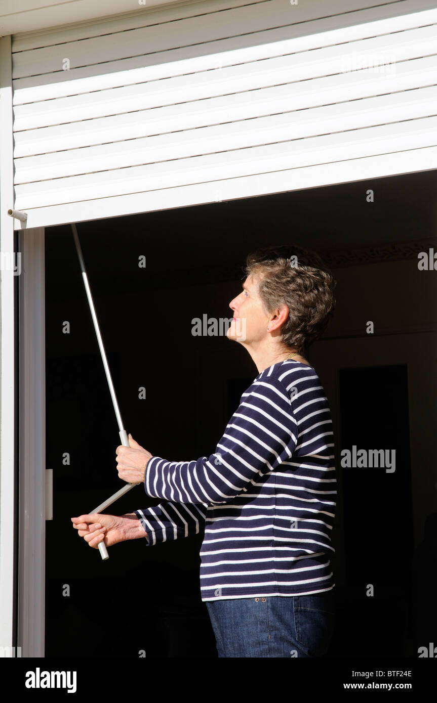Woman closing metal security shutters on the ground floor of her home ...