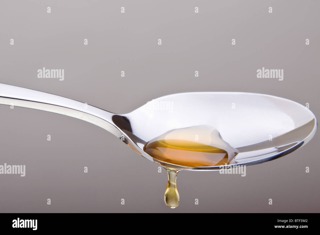 Thick sweet honey dripping off a silver spoon Stock Photo - Alamy