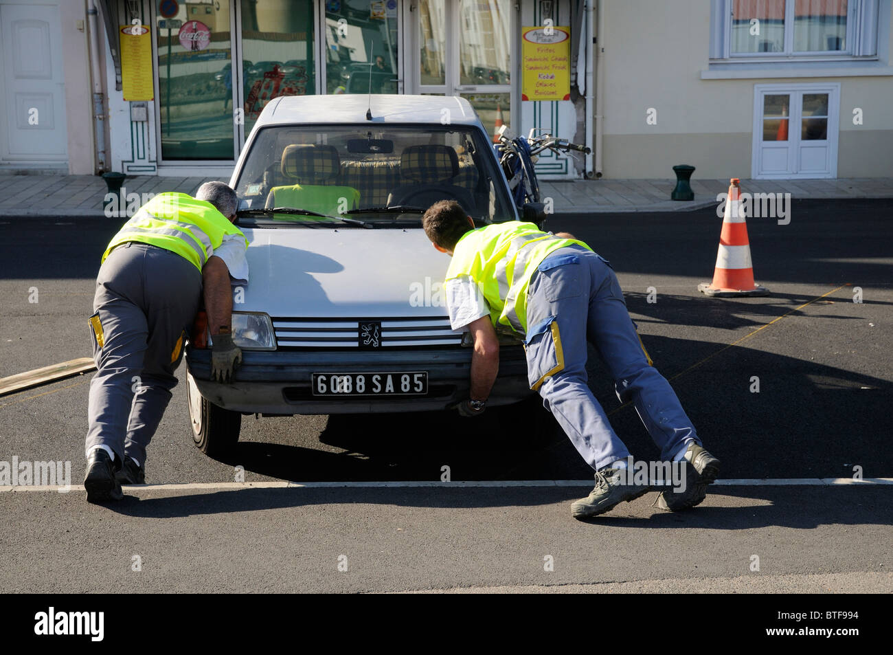 Two workmen forcibly move a car to enable them to paint white lines in ...