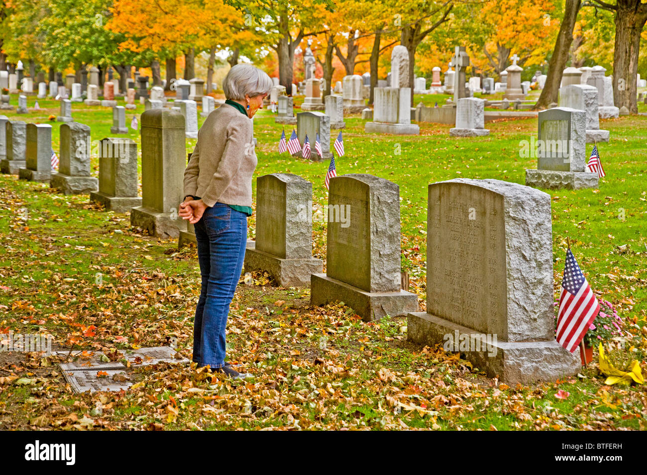 A woman visits her parents' grave in a cemetery on an autumn afternoon ...