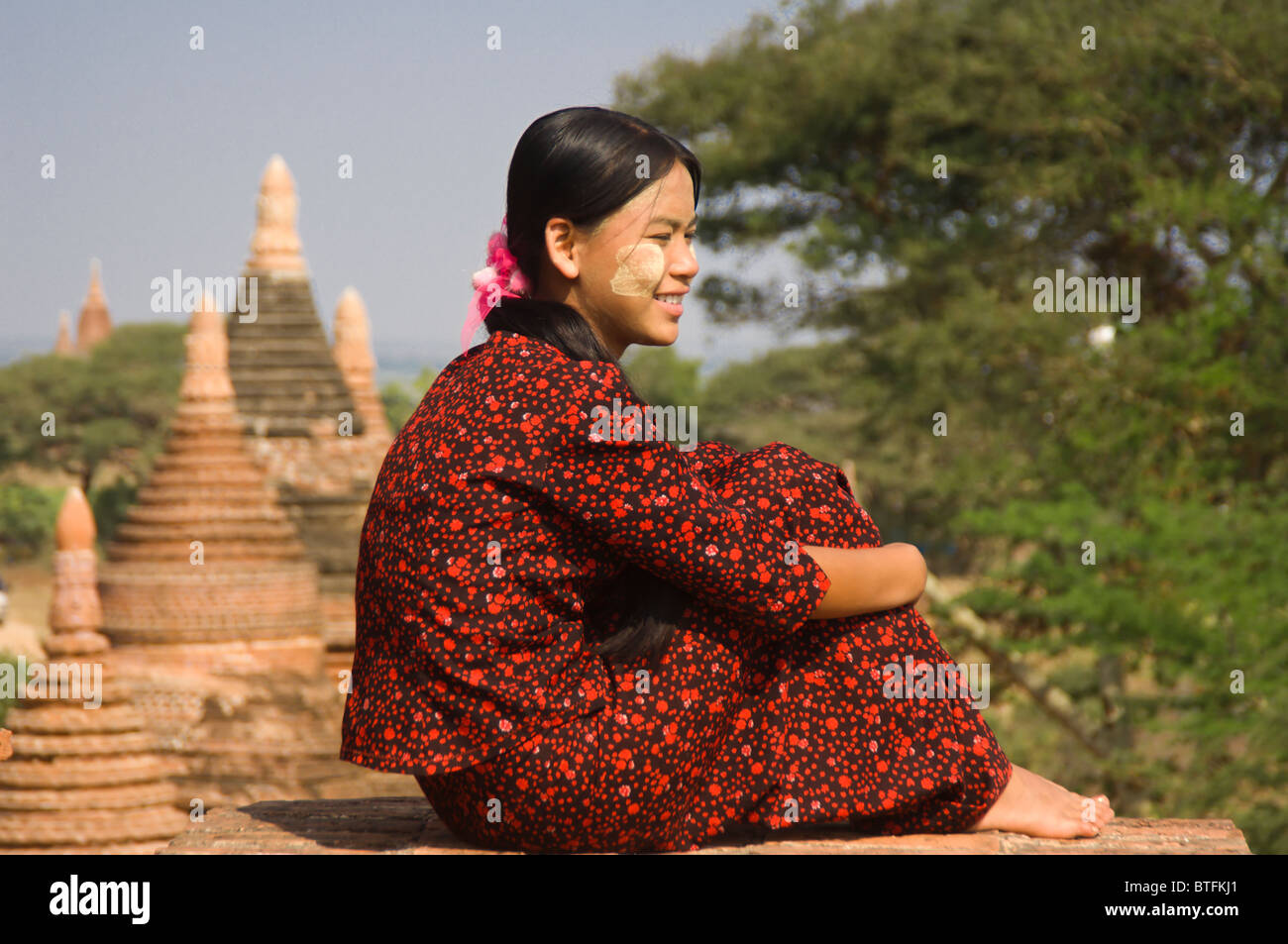 Young Burmese woman in a red dress sitting on the roof of a temple ...