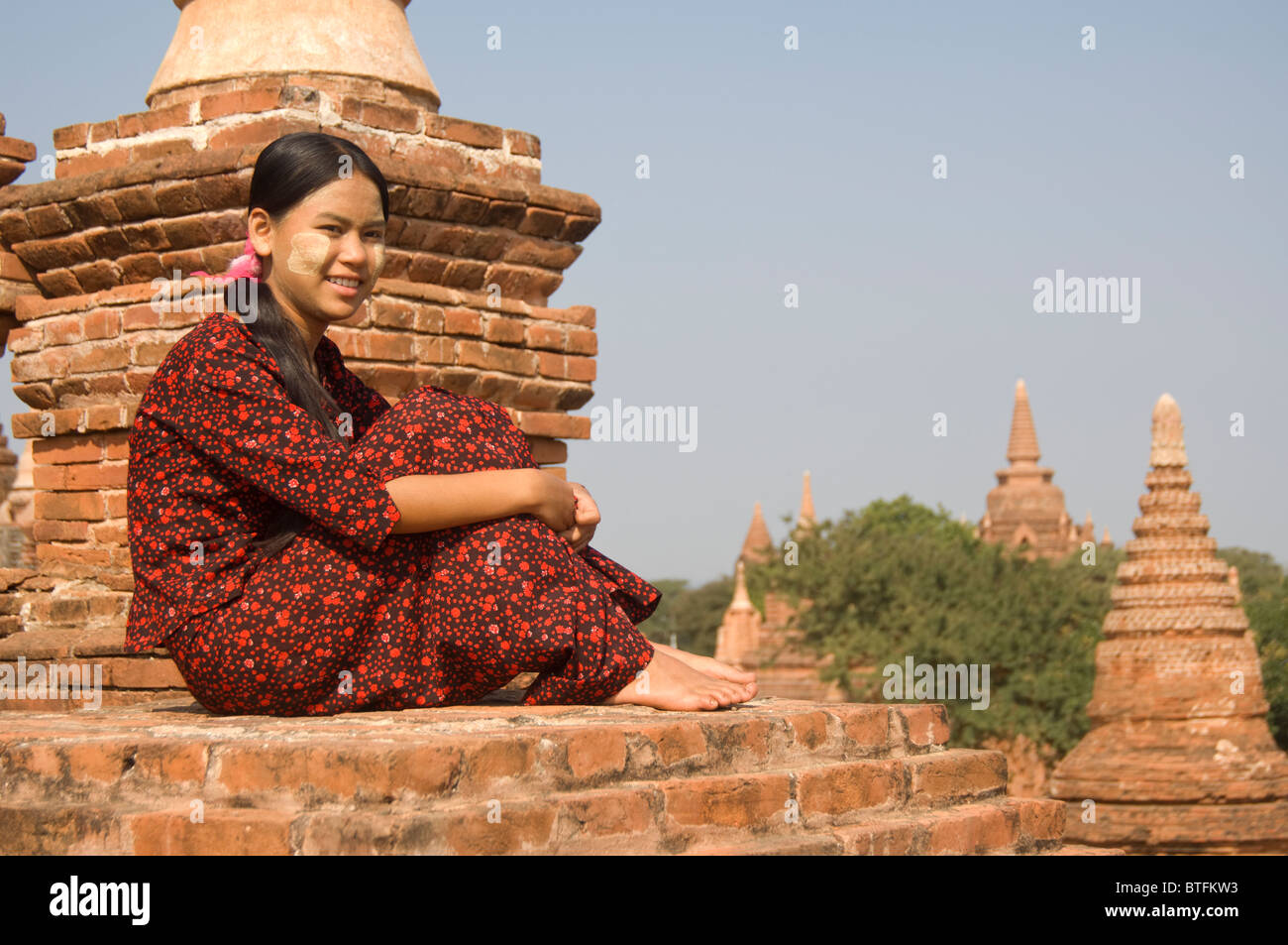 Young Burmese woman in a red dress sitting on the roof of a temple ...