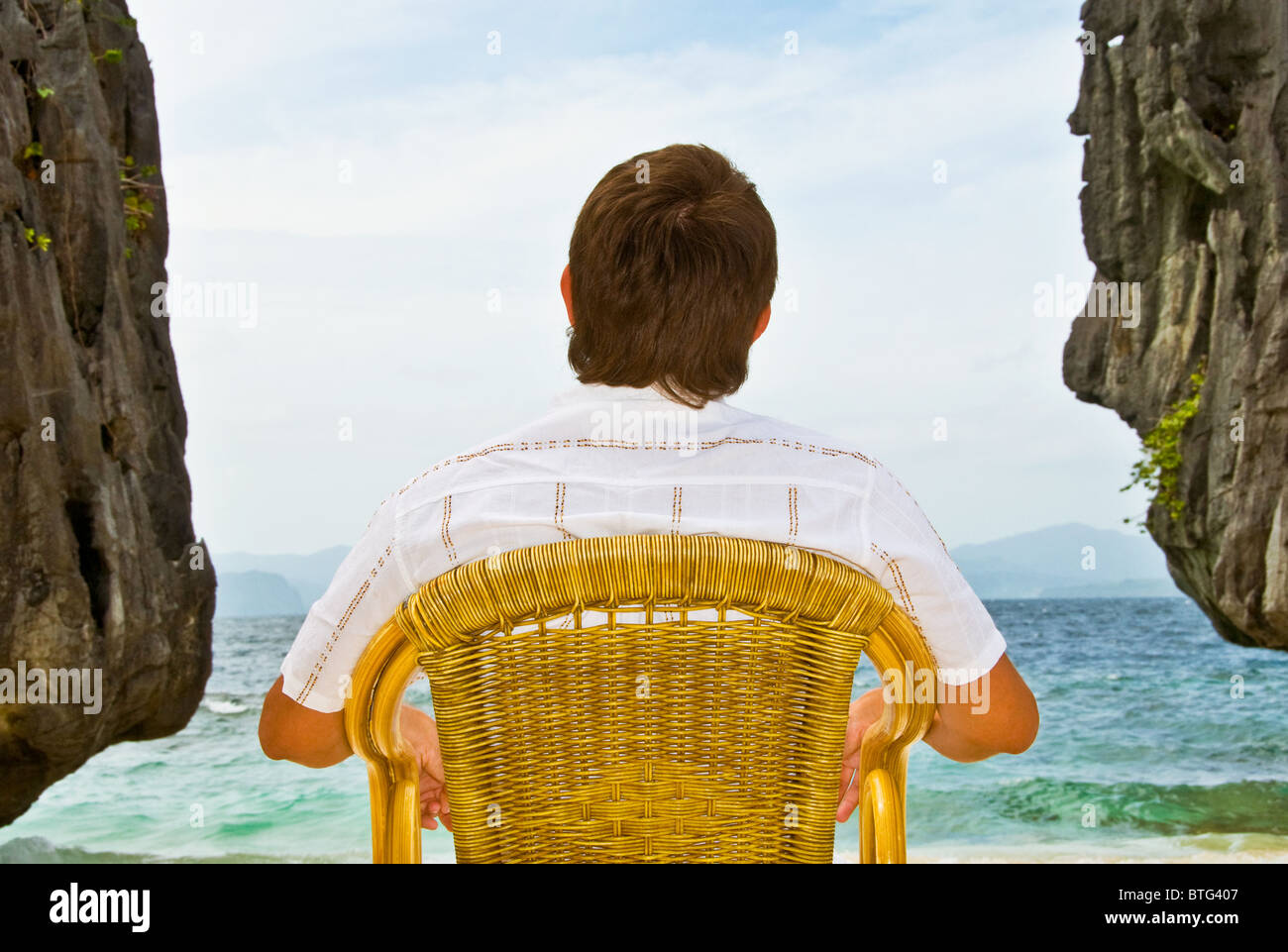 Man sitting between two rocks looking in to the ocean Stock Photo - Alamy