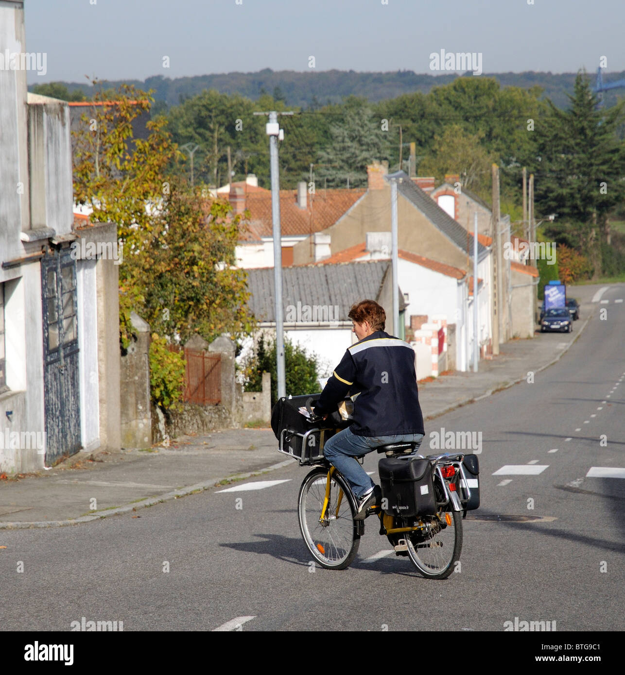 French postwoman riding her yellow painted bicycle in the rural town of ...