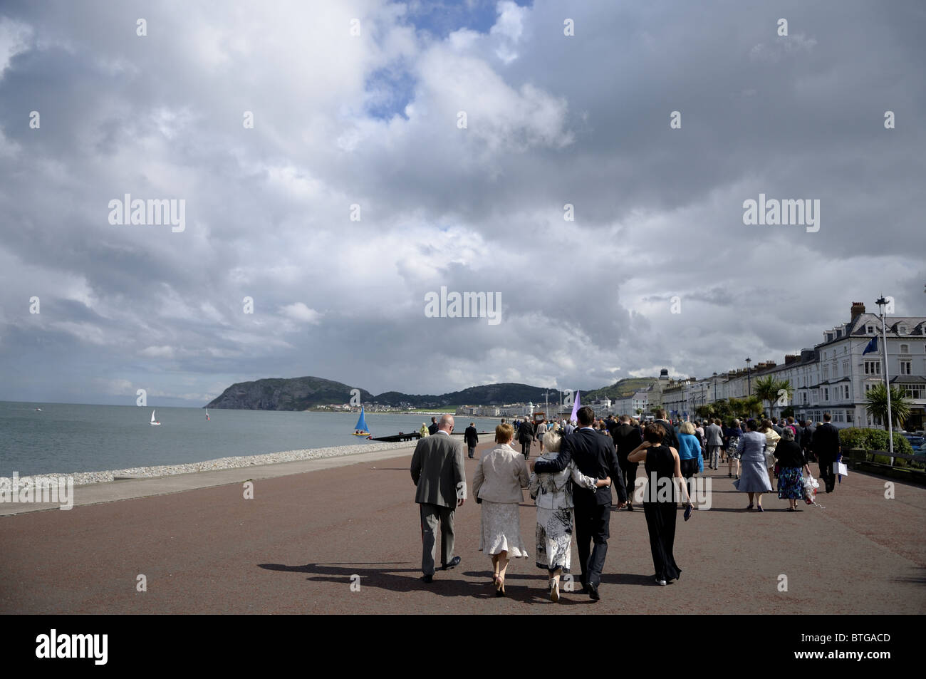 Wedding guests walk along the prom at Llandudno Stock Photo - Alamy