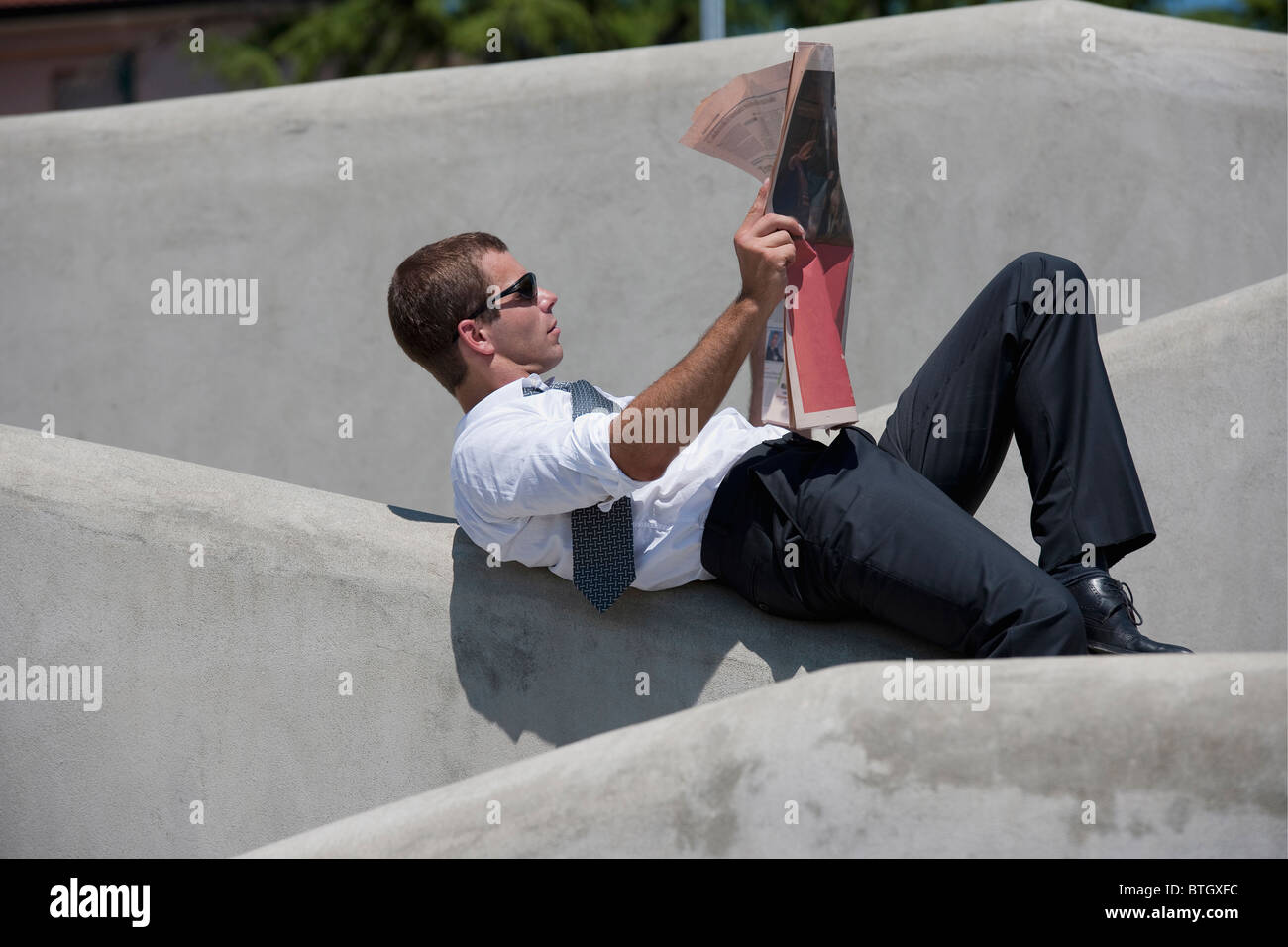 Man lying down on wall reading newspaper Stock Photo - Alamy