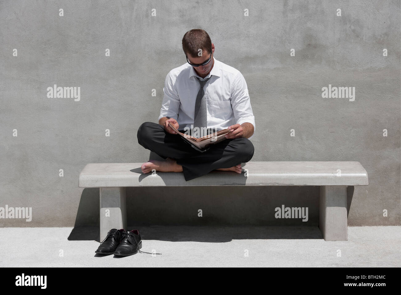 Barefoot businessman sitting on bench reading newspaper Stock Photo - Alamy