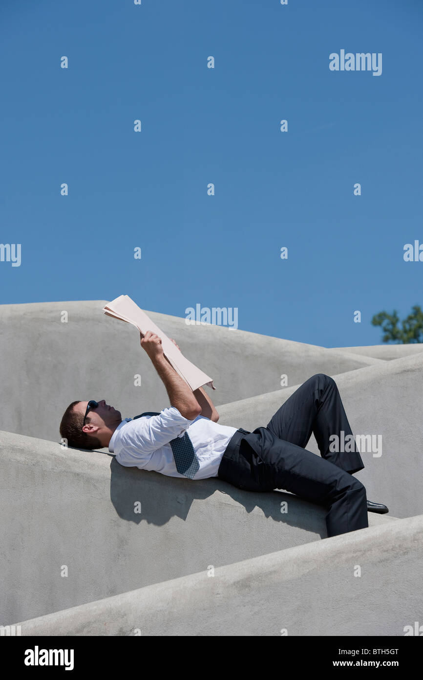 Man lying down on wall reading newspaper Stock Photo - Alamy
