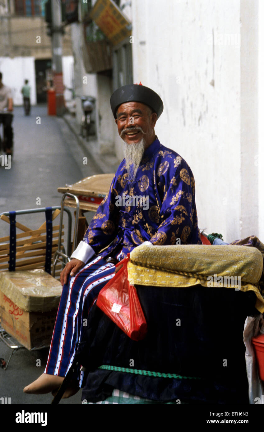 A Chinese man dressed in a traditional Chinese outfit smiles in an old ...