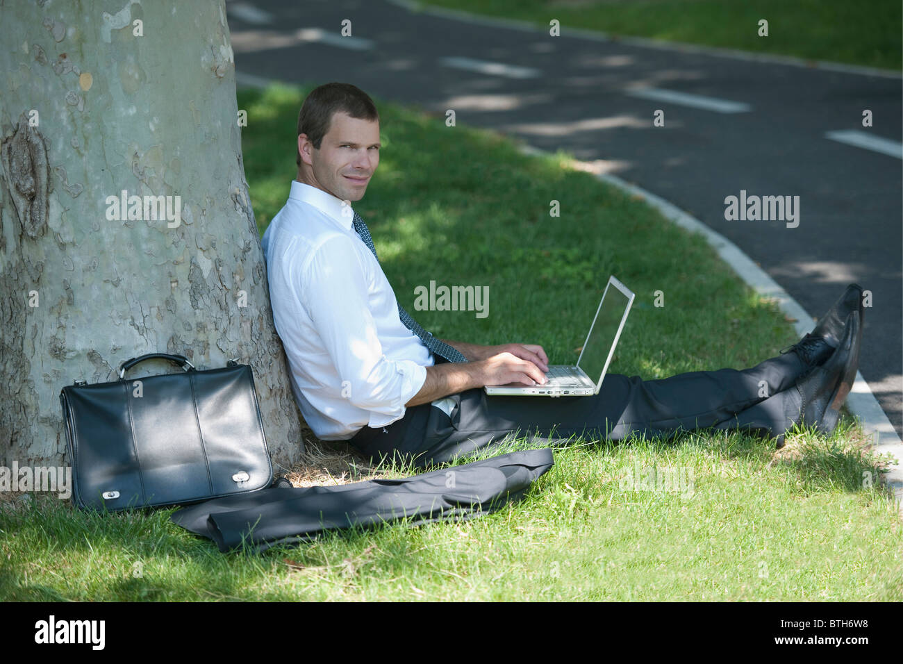 Businessman with laptop working under a tree Stock Photo - Alamy