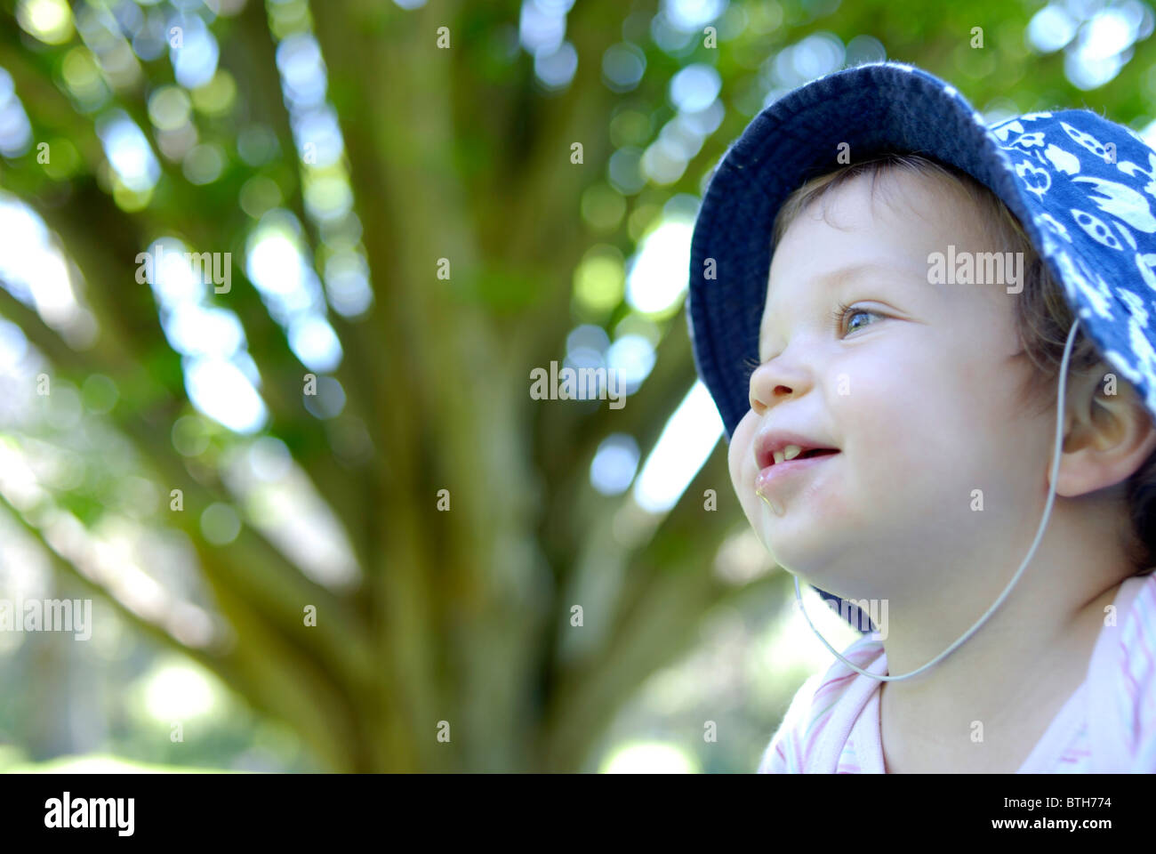 One year old baby outside in summer in shade of tree and wearing a sun ...