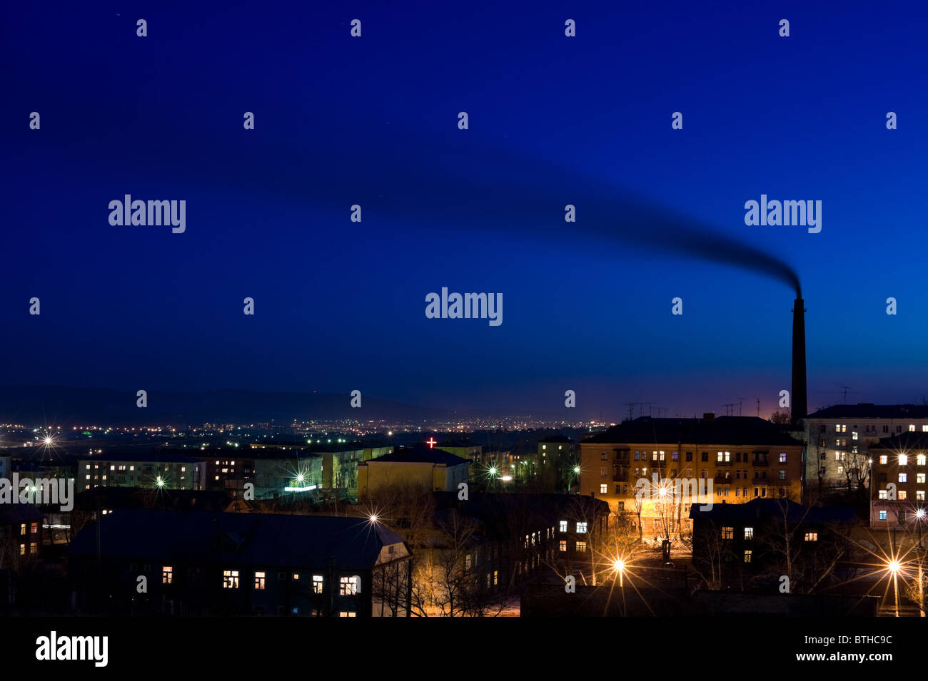 tall smokestack belches smoke into sky over night city, copy space ...
