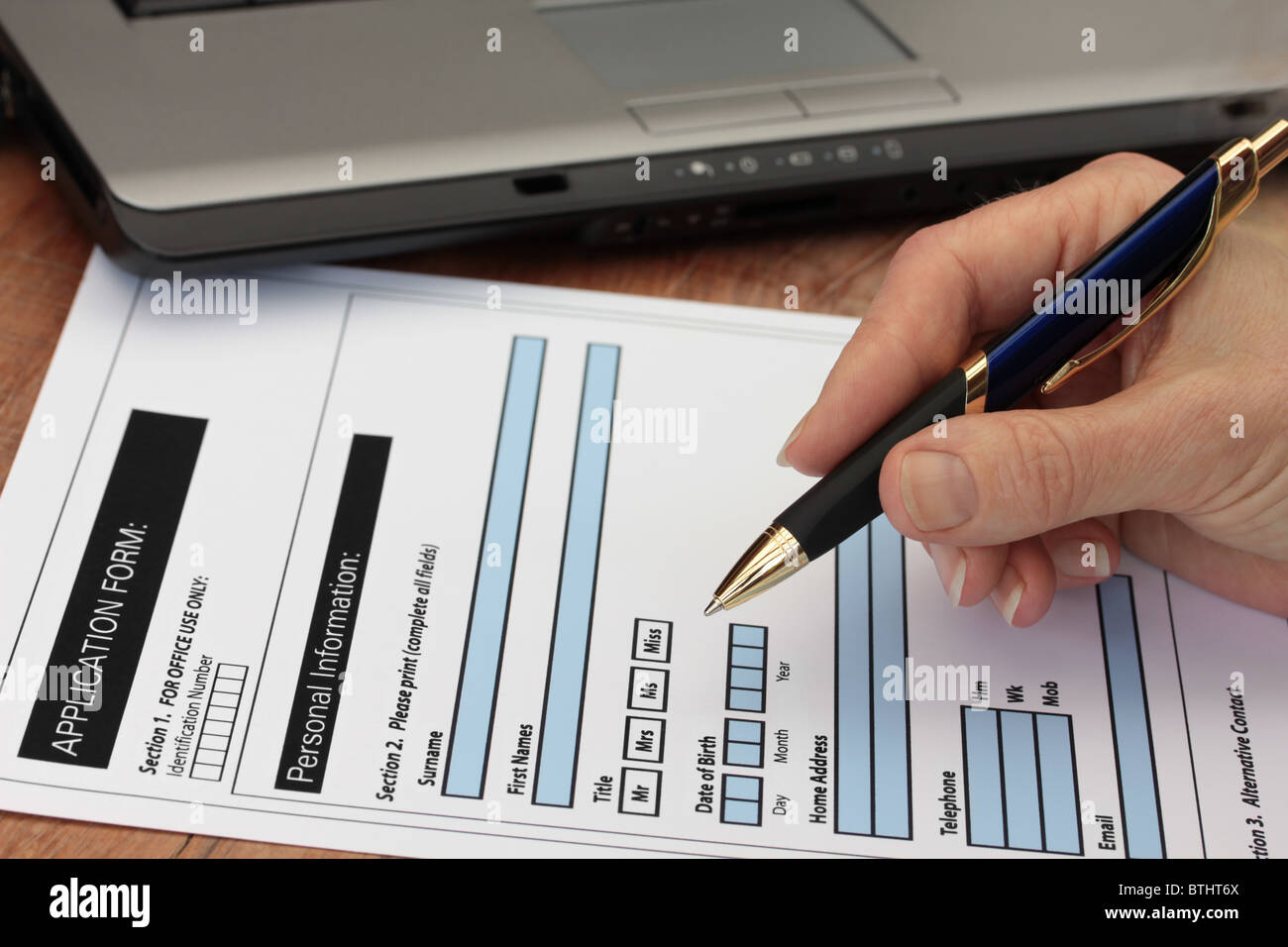 Hand with Pen Completing Fictitious Form with Laptop in Background ...