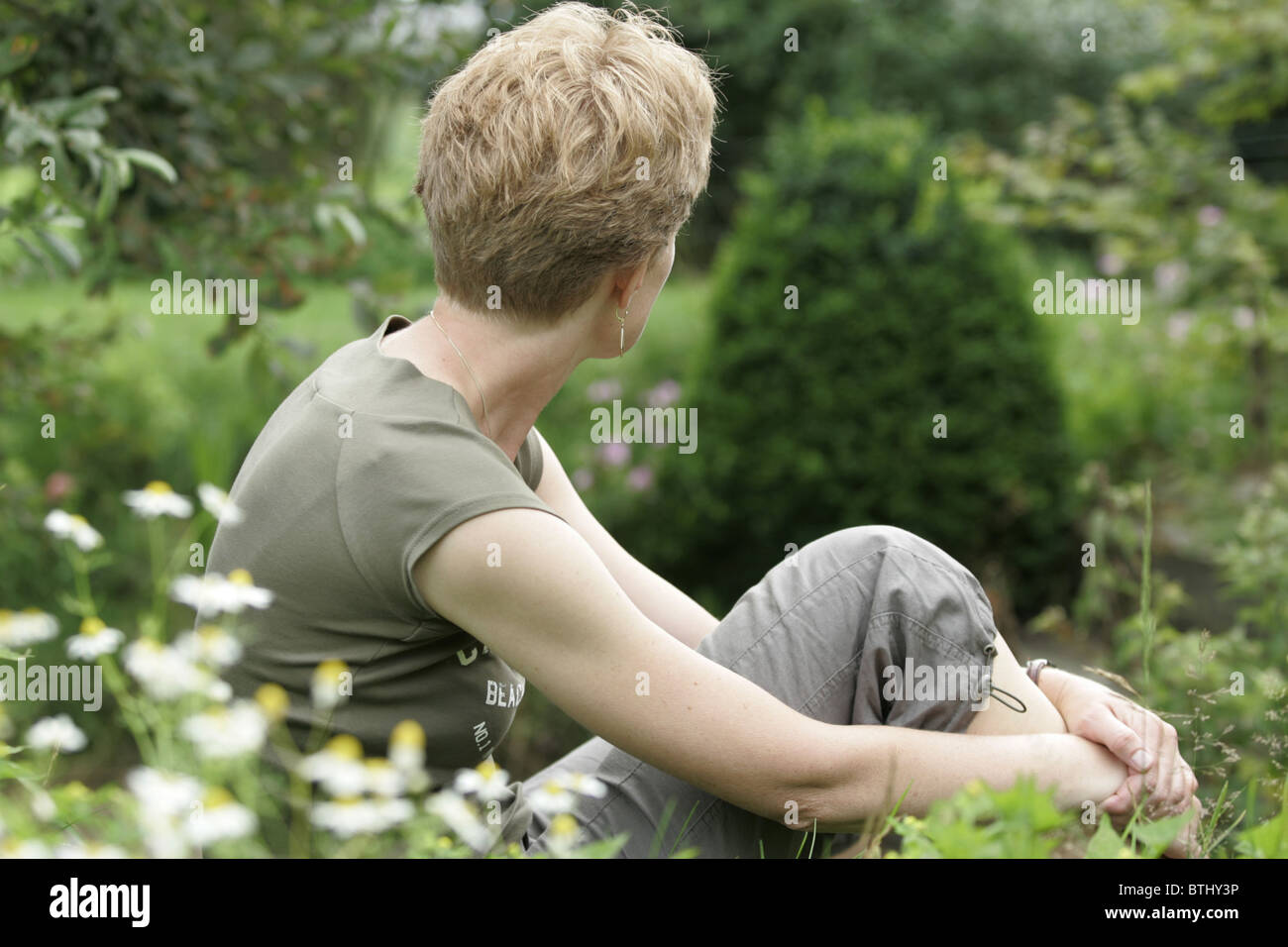 Anonymous woman alone outdoors sit in garden thinking Stock Photo - Alamy