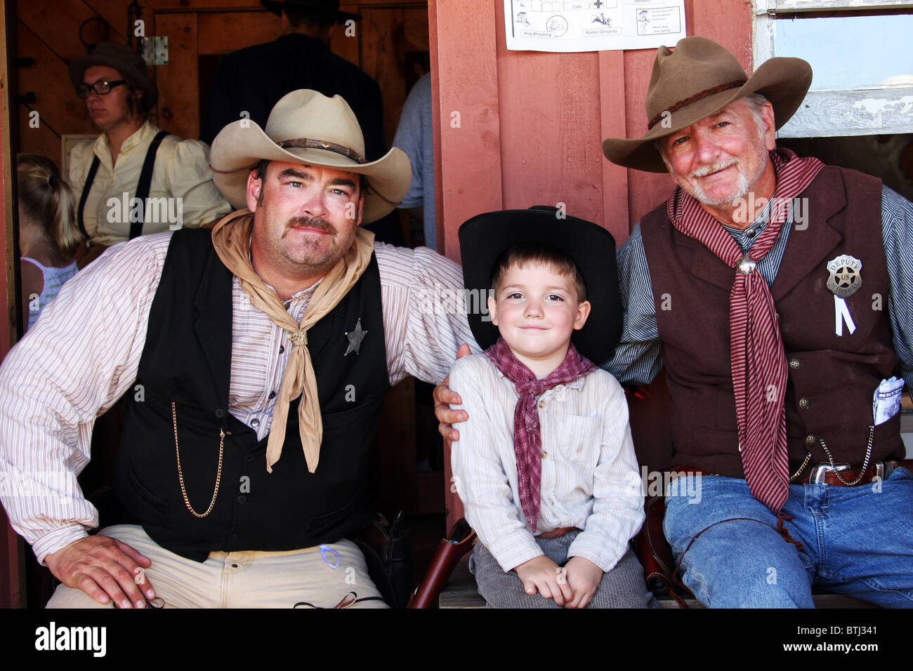 Two mature cowboys and a young child cowboy sitting on a bench at an ...