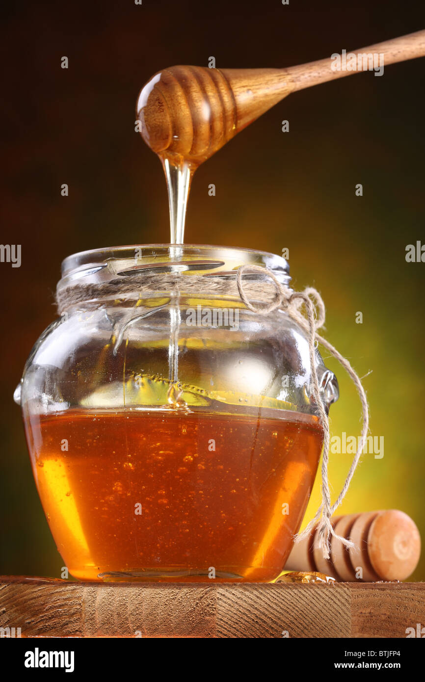 Sweet honey pouring from drizzler into the pot. Pot is on wooden table ...