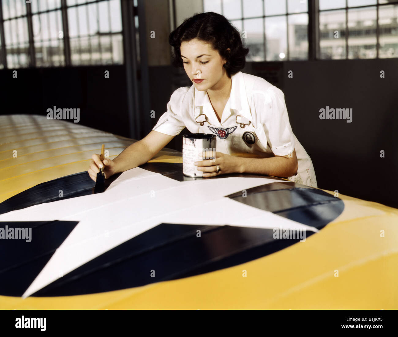 Civil service worker paints the American insignia on a US Navy airplane ...