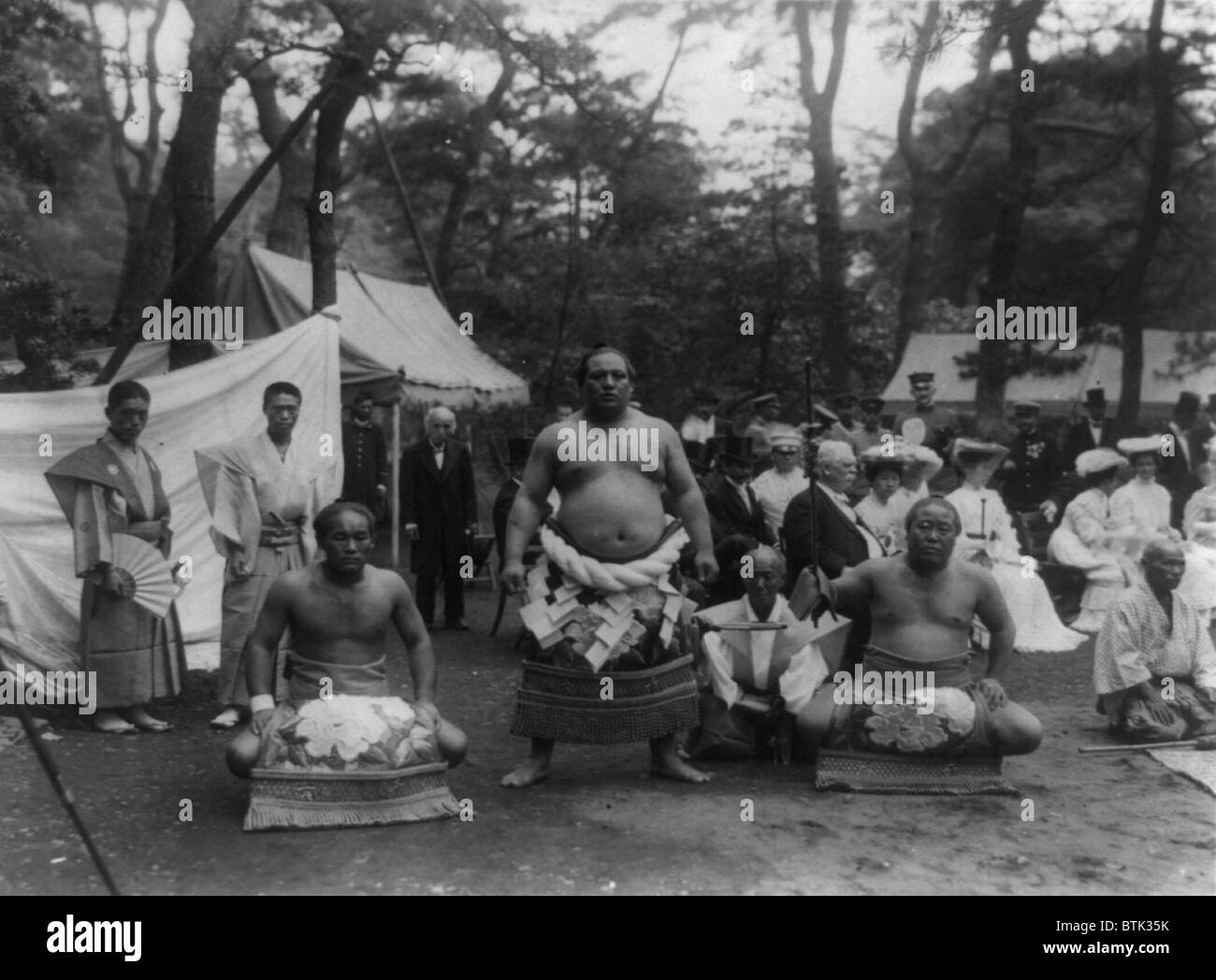 Three sumo wrestlers posed outdoors with spectators in background ...