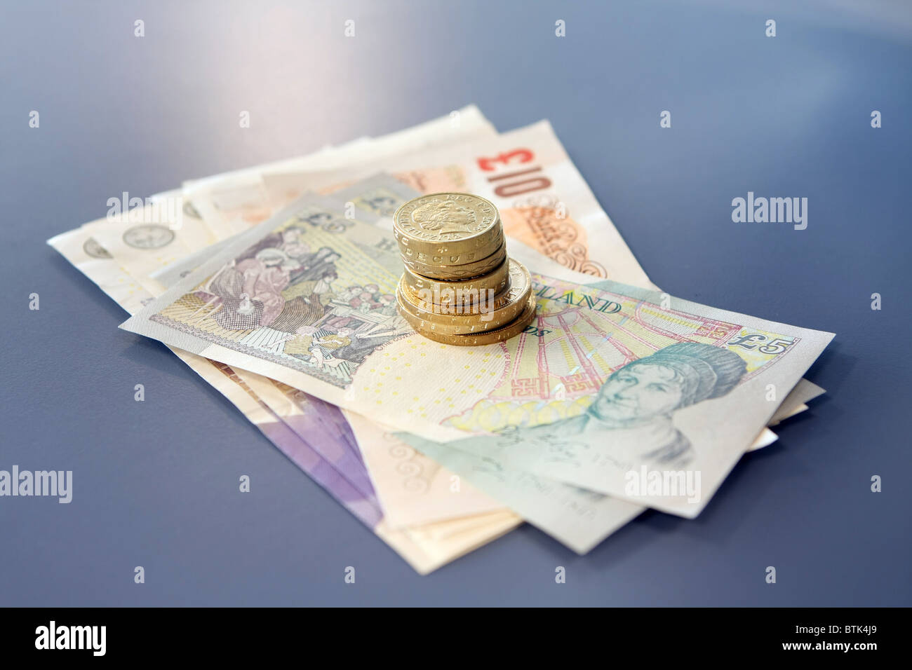A stack of sterling £2 and £1 coins on a pile of £5, £10 and £20 notes ...
