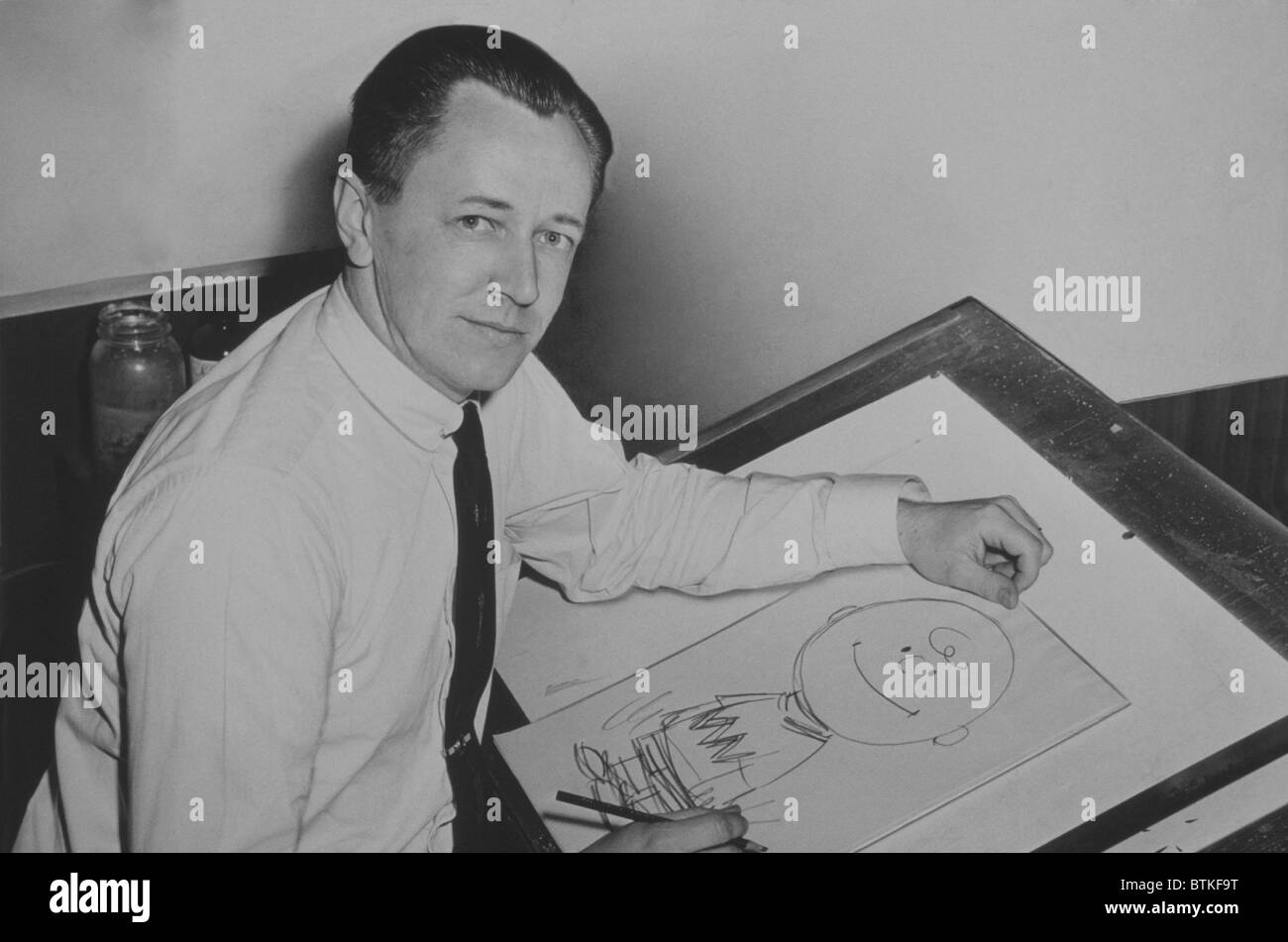 Charles Schulz (1922-2000), seated at drawing table with drawing of ...