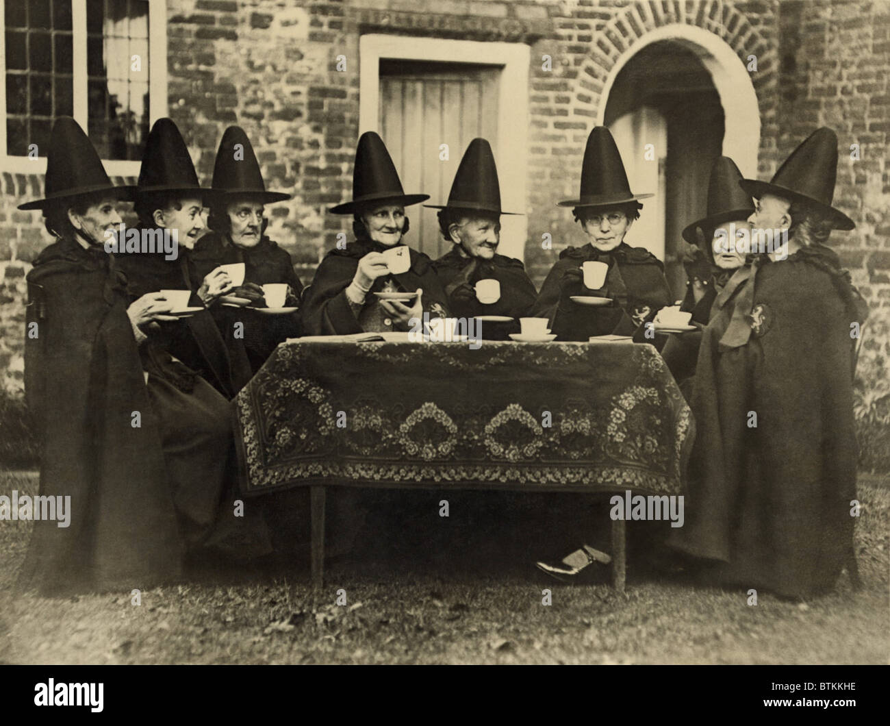Eight women in high hats having tea. They are not a group of witches ...