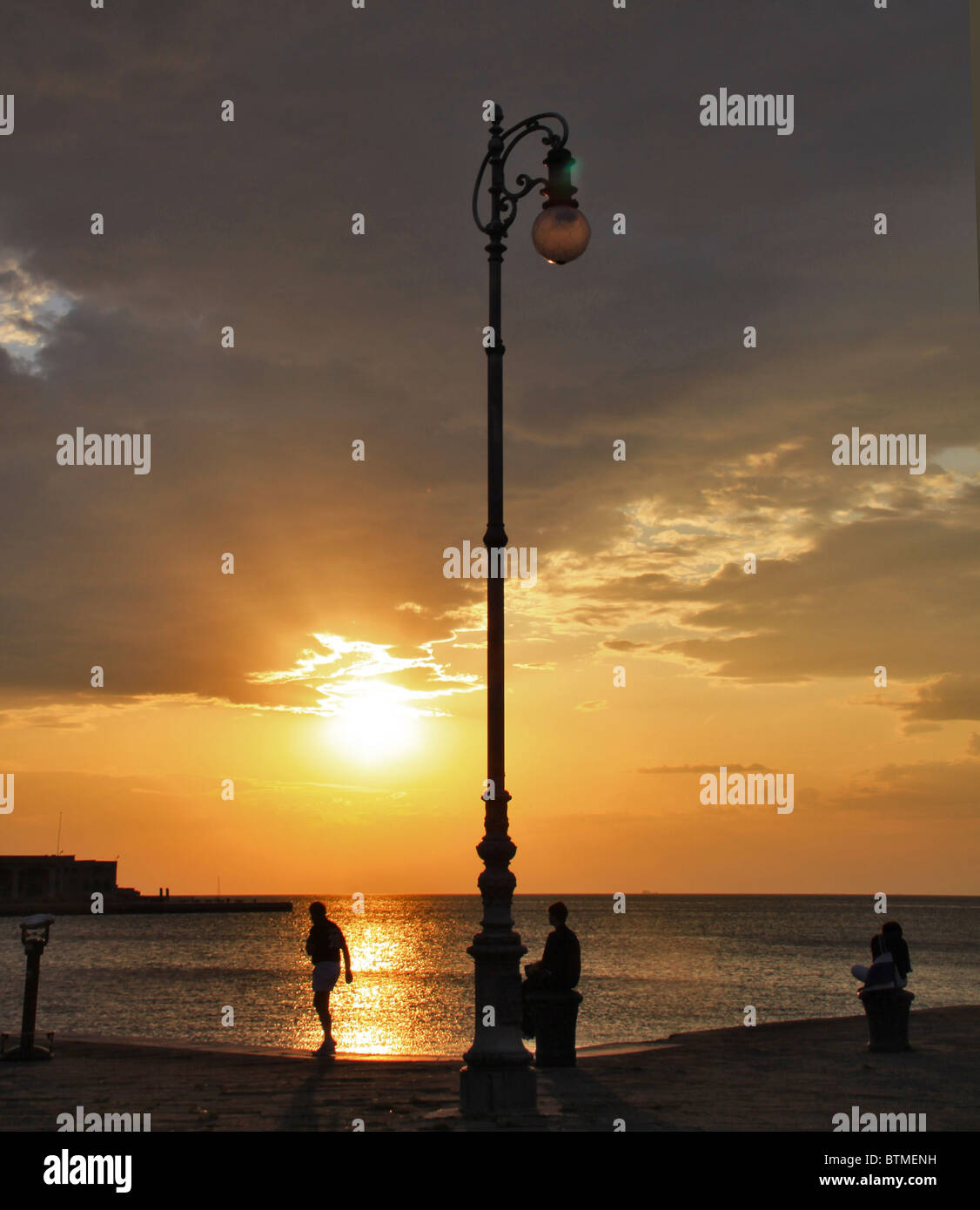 Trieste harbor, sunset on the sea with a street lamp against clouds ...