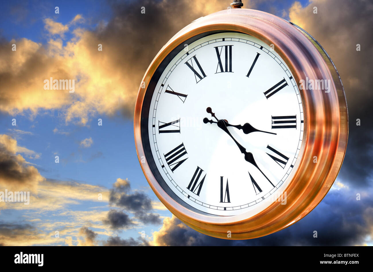 Copper clock face in sun setting sky with gold, yellow and blues clouds ...