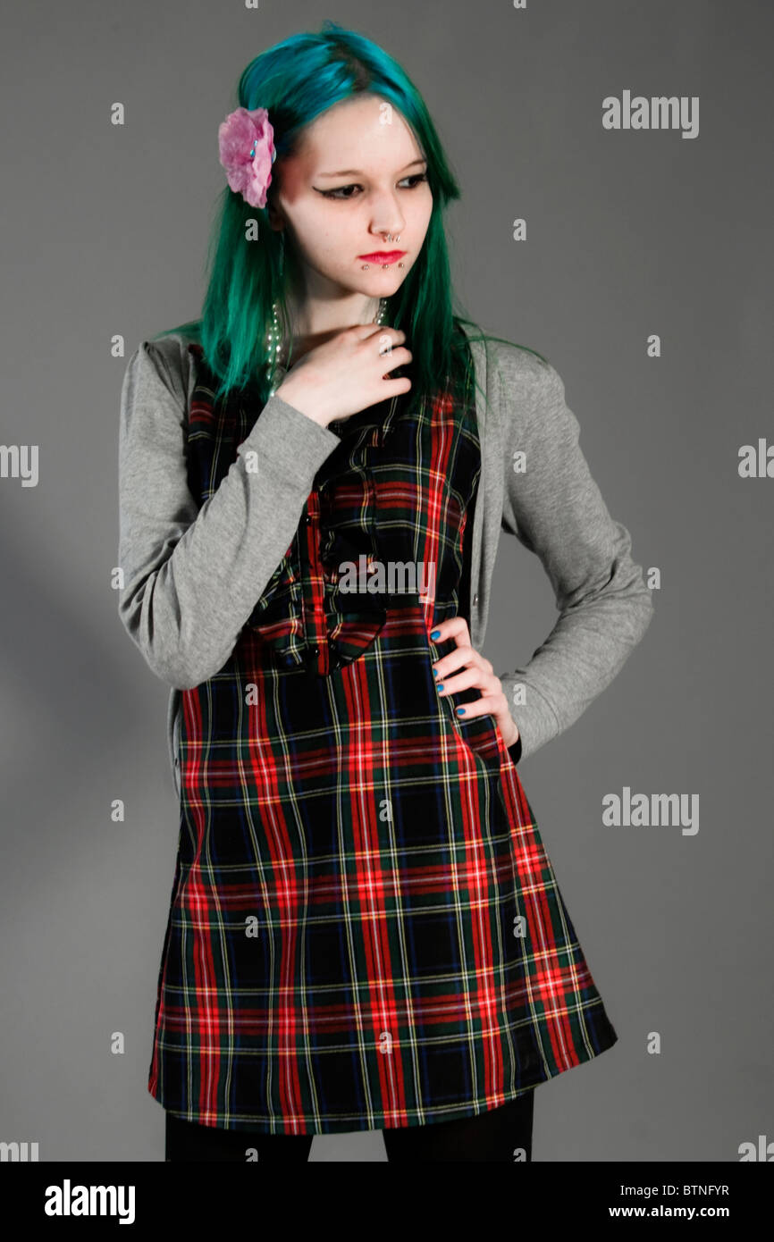 A young goth woman with green hair in a plaid dress and cardigan on a ...