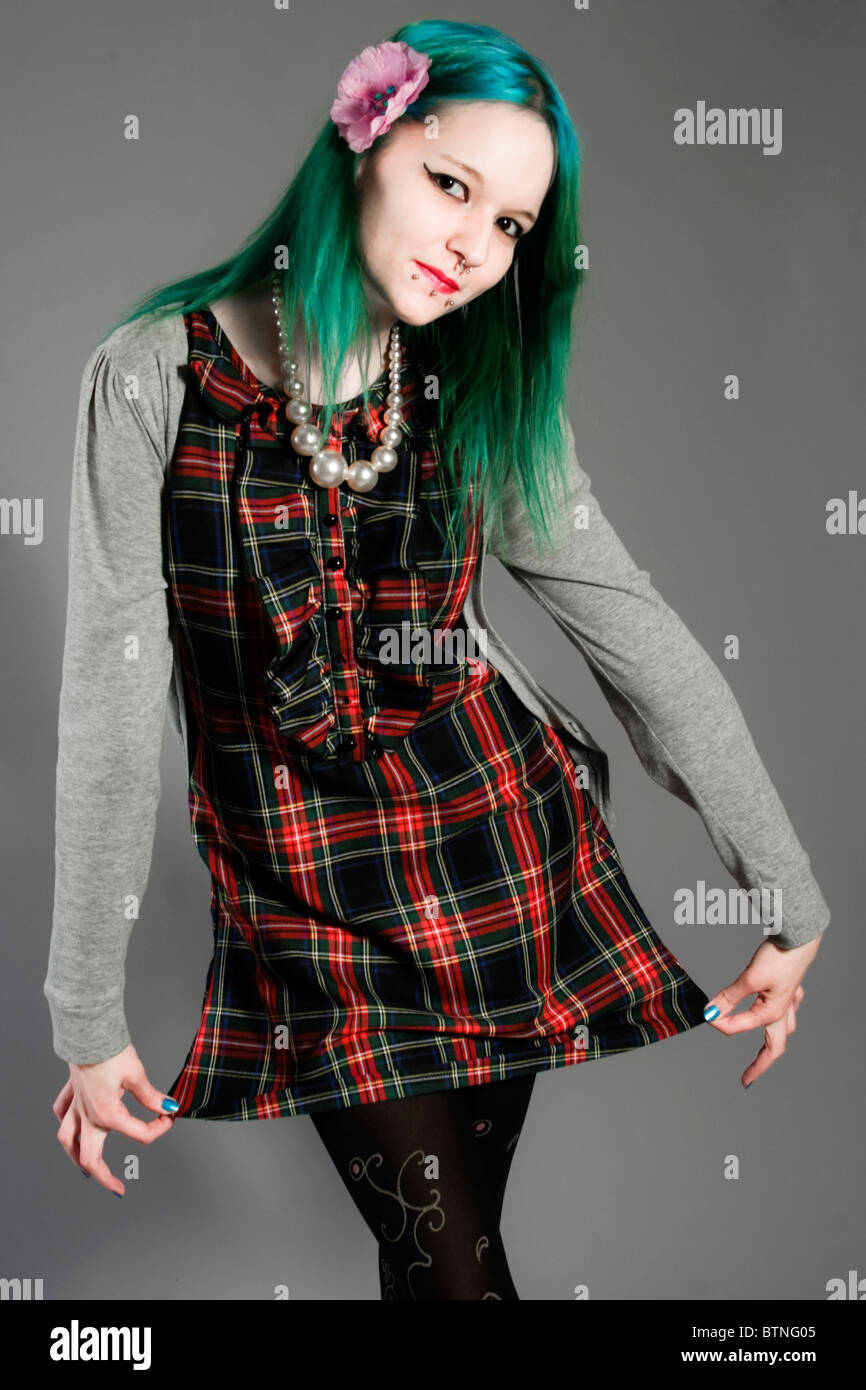 A young goth woman with green hair in a plaid dress and cardigan on a ...