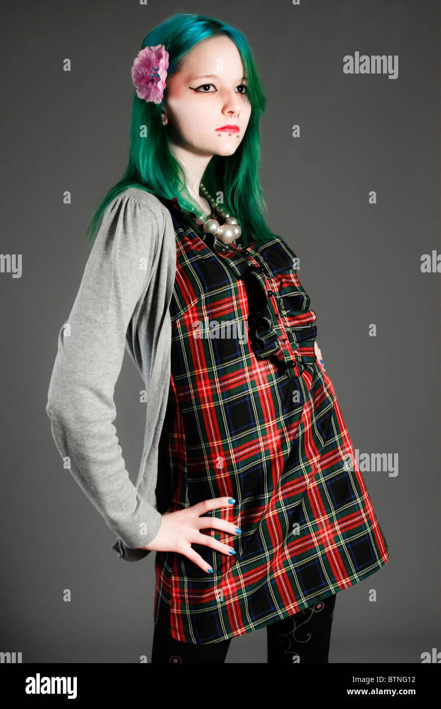 A young goth woman with green hair in a plaid dress and cardigan on a ...