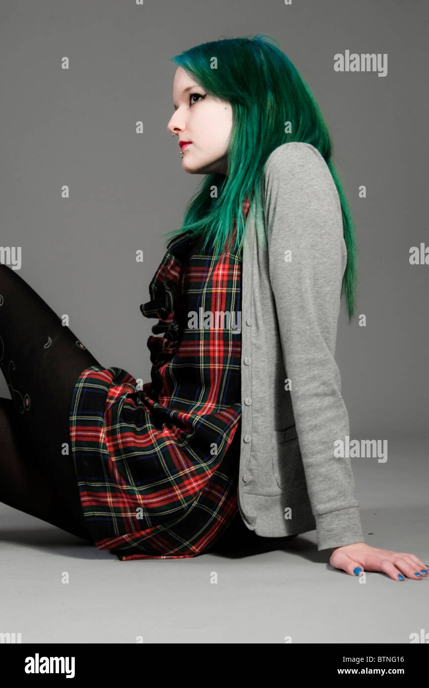 A young goth woman with green hair in a plaid dress and cardigan on a ...