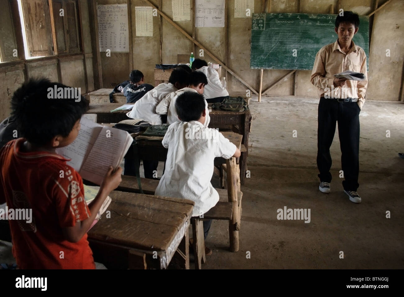 A teacher is reading a Lao language book while his students follow ...