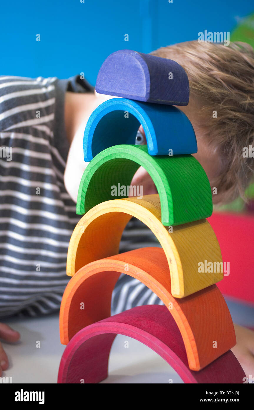 Young boy (8-10 years) pearing through coloured wooden building blocks ...