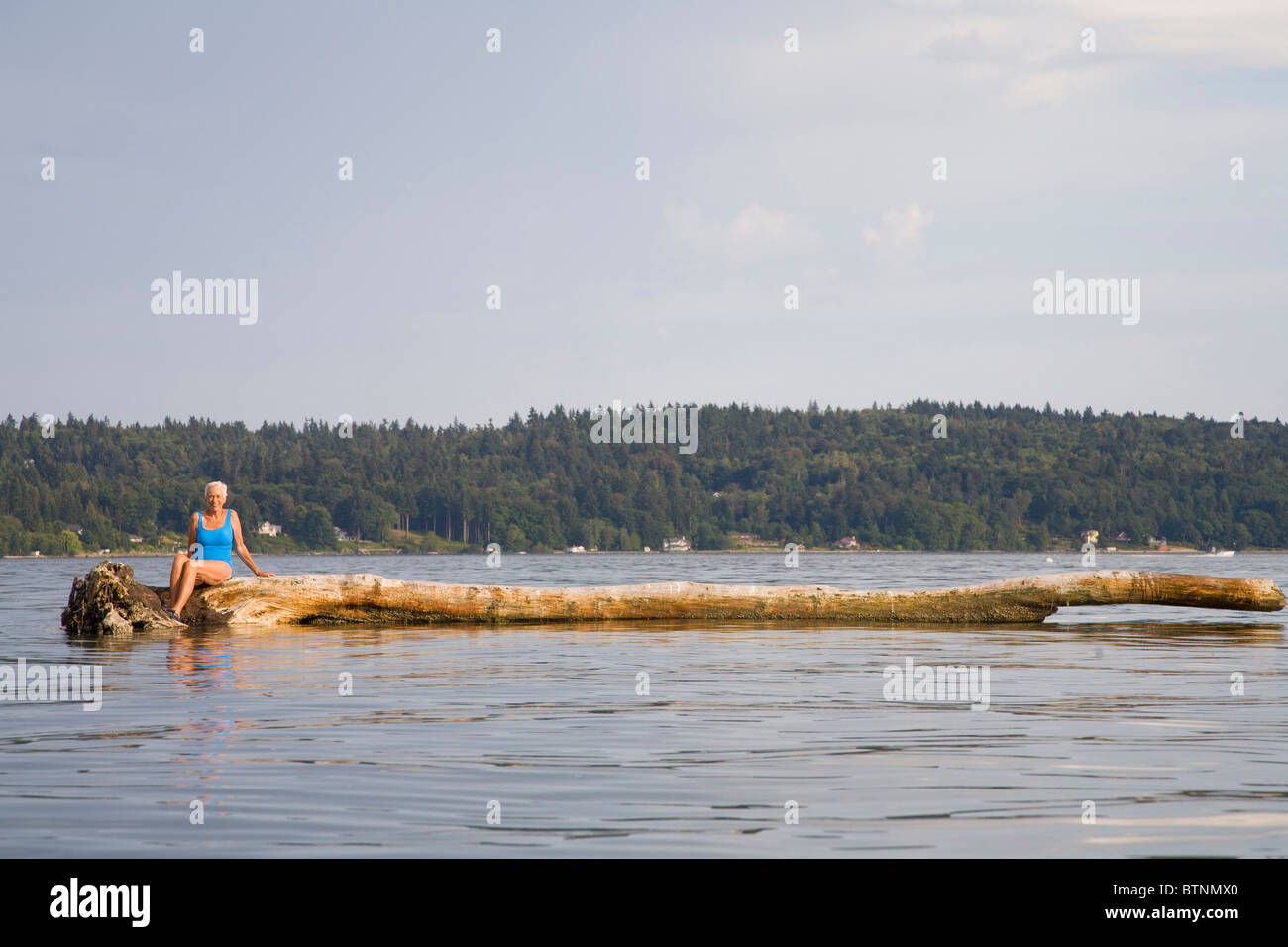 Senior woman sitting on floating log Stock Photo - Alamy