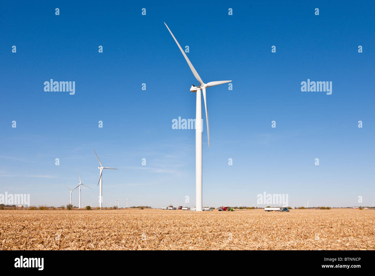 Farmers harvesting corn under wind turbine in corn field near Brookston ...
