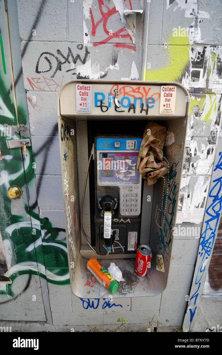 A vandalized and neglected public telephone booth covered with graffiti ...