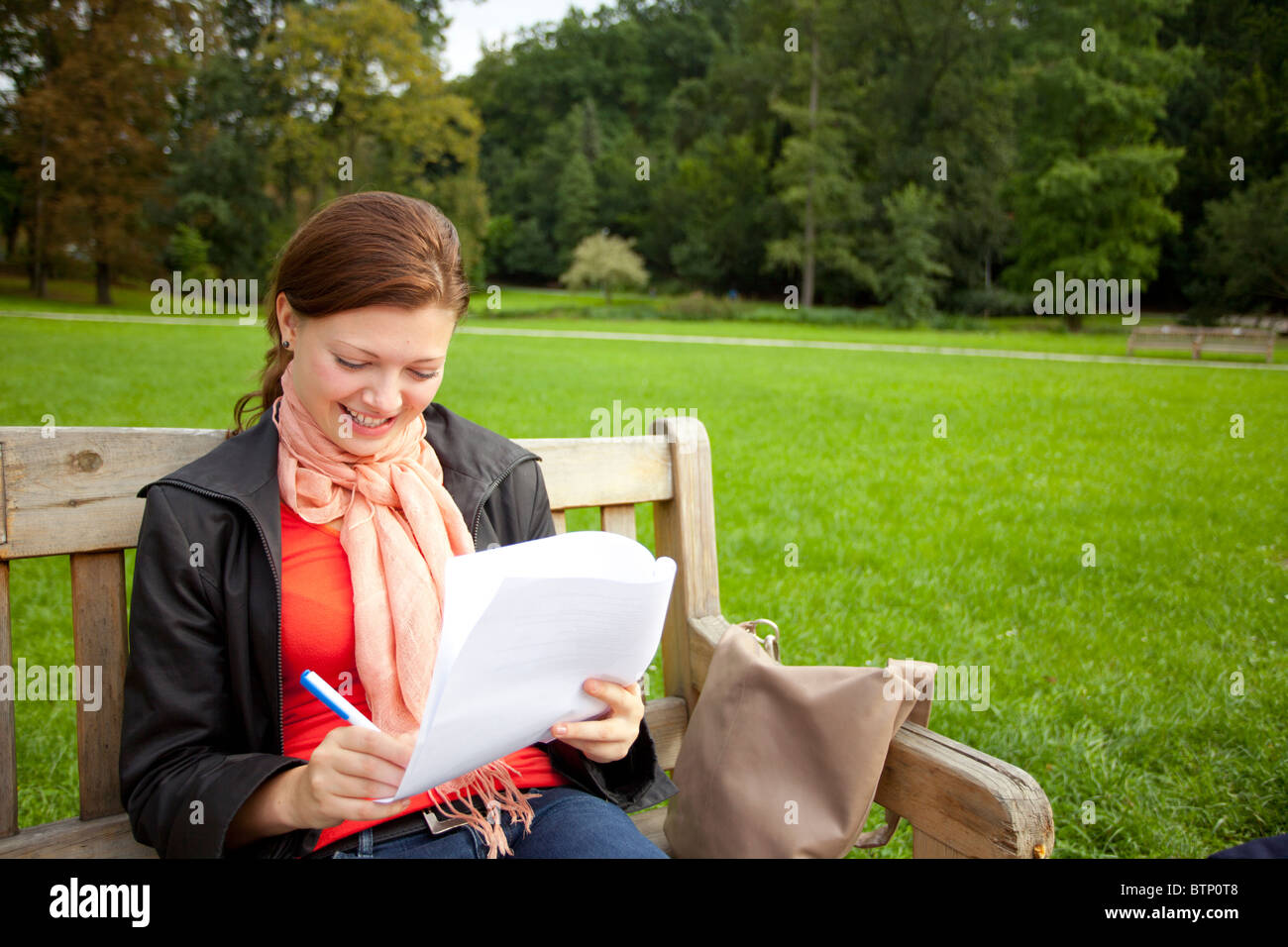 Woman sitting on a park bench, smiling while writing in a notebook ...
